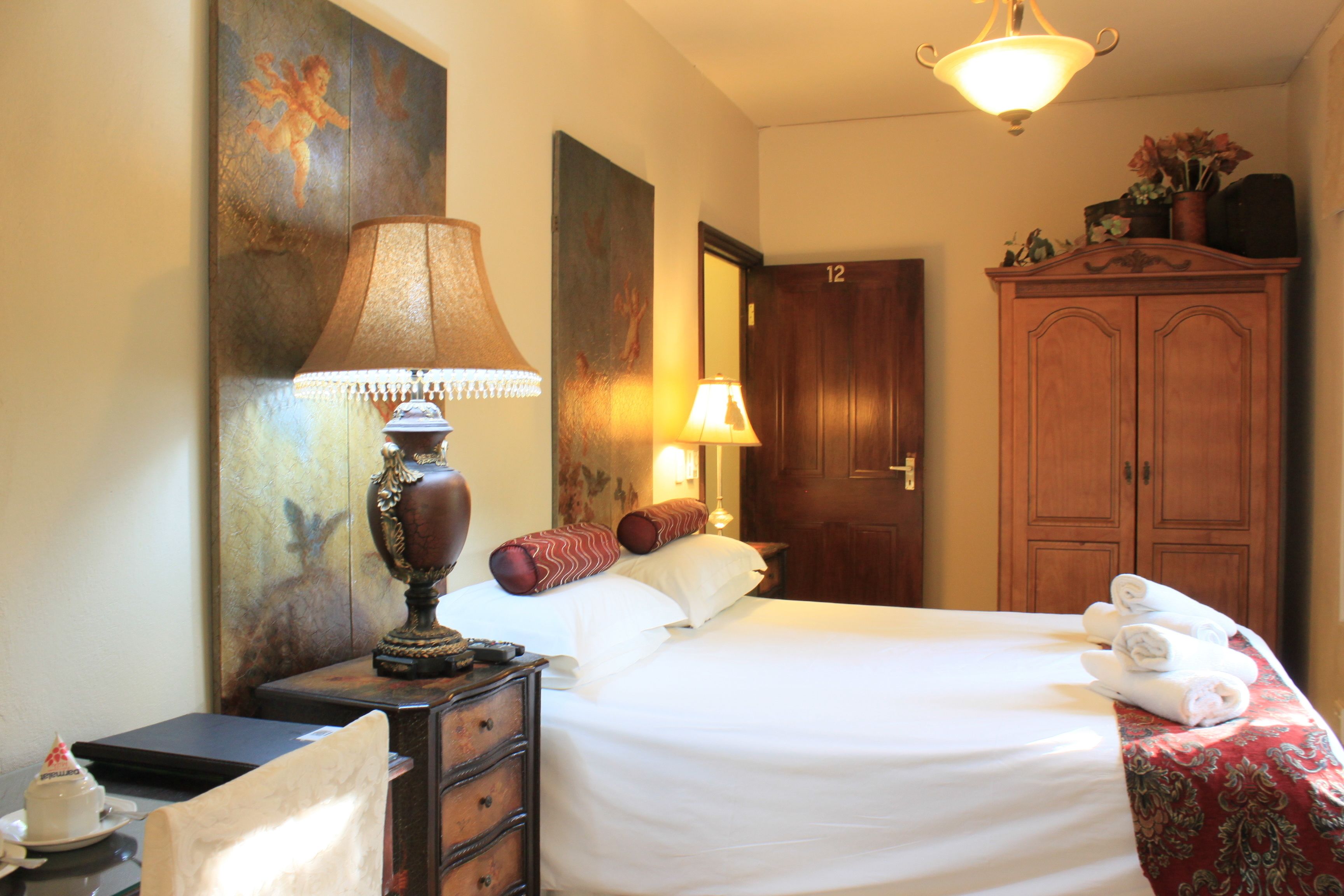 Quarto de hotel com cama, cômoda, abajur e porta.
