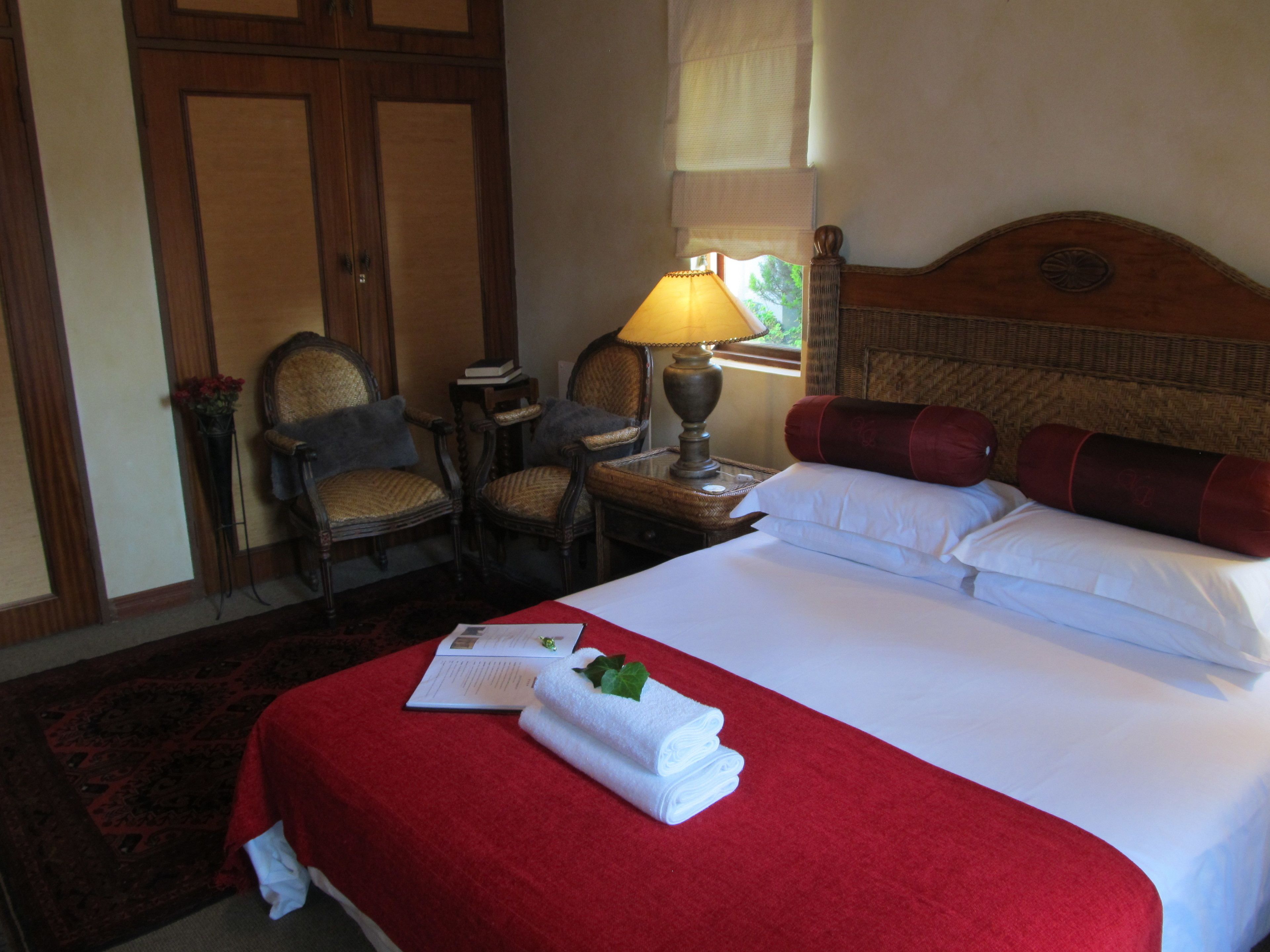 Quarto de hotel com uma cama grande, duas cadeiras, uma mesa de cabeceira e uma janela com cortinas.