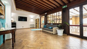 Uma sala de estar espaçosa com piso de madeira, um sofá com almofadas, uma mesa de centro, uma estante de livros e uma janela grande com vista para o exterior.