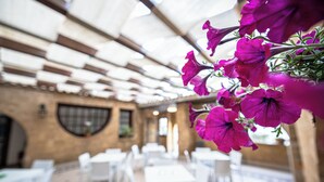Um restaurante com mesas e cadeiras brancas, parede de tijolos e teto com vigas de madeira.