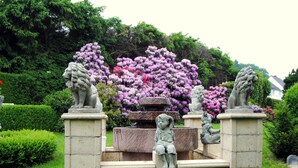 Um jardim com uma fonte, estátuas e flores cor-de-rosa em flor.