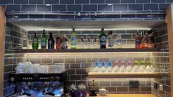 Uma área de bar com uma máquina de café, prateleiras de garrafas de bebidas e diversos copos.