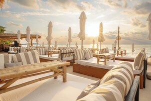 Uma área de lounge à beira-mar com almofadas listradas, móveis de madeira e guarda-sóis.
