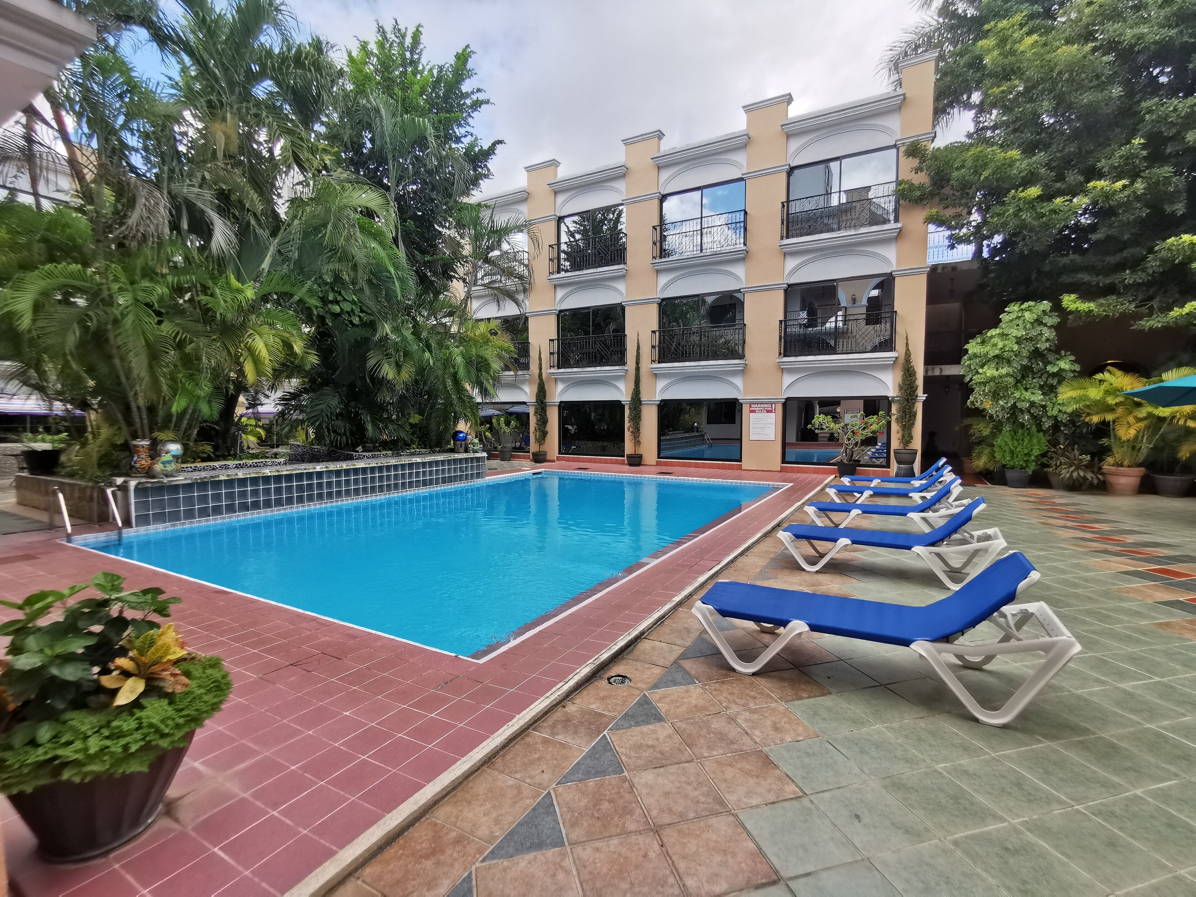 Uma área de piscina com deck revestido, cadeiras de descanso e plantas em vasos.