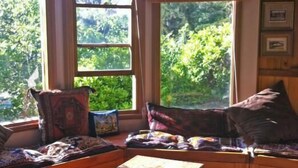 Um quarto acolhedor com um banco de madeira, um pequeno baú de madeira e uma janela grande com vista para o verde.