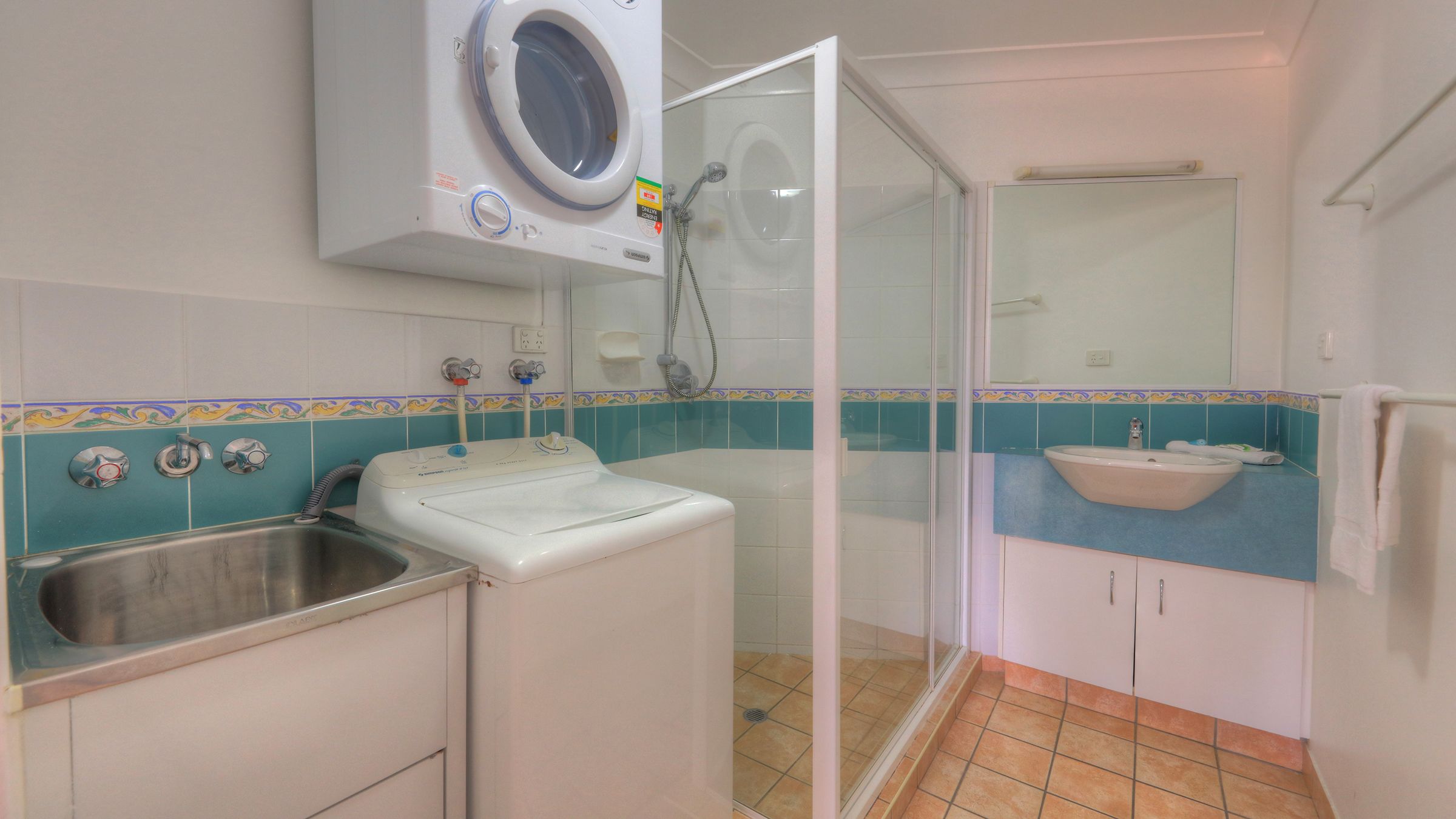 Casa de banho compacta com máquina de lavar, lavatório e chuveiro.