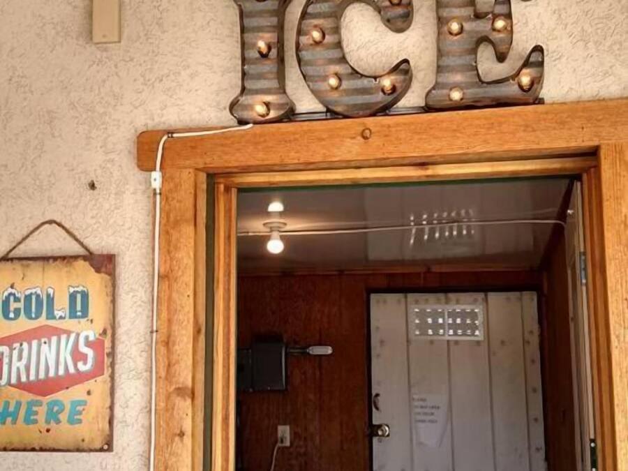 Uma porta de madeira com uma placa acima que diz 'ICE' e outra placa à esquerda que diz 'BEBIDAS FRIAS AQUI'.