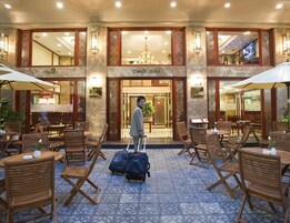 Um saguão de hotel com área de estar central, balcão de recepção e restaurante e bar visíveis.