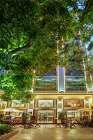 Hotel com área externa para sentar, espaço coberto e prédio de vários andares com janelas iluminadas.