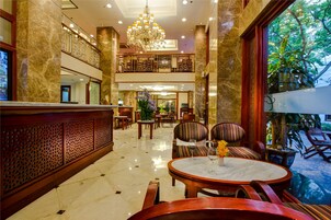 Um hall de hotel com piso de mármore, um candelabro, um balcão de recepção e uma área de estar com cadeiras listradas.