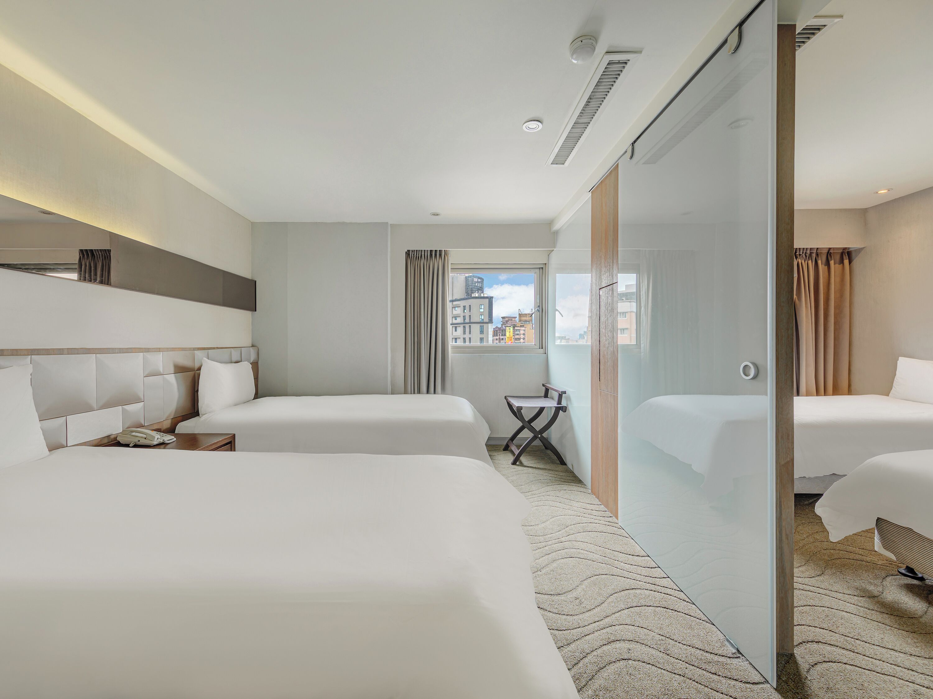 Quarto de hotel com duas camas, uma mesa pequena e vista para a cidade.