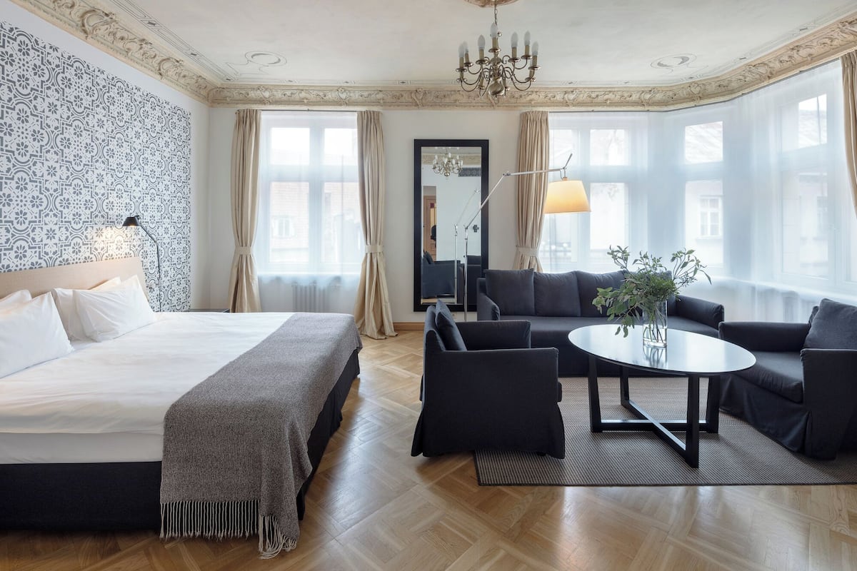 Quarto de hotel com uma cama grande, um sofá, uma mesa de centro e um candelabro.