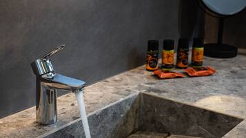 Um banheiro moderno com uma torneira cromada, bancada de mármore e três frascos de produtos de higiene laranja.
