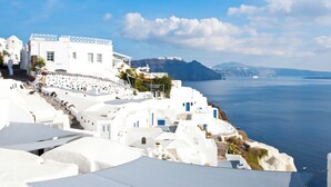 Uma vila costeira com edifícios brancos, um céu azul límpido e vista para o mar.