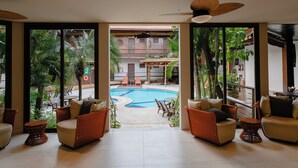 Espaçoso espaço interno com móveis de vime, piscina e amplas janelas com vista para um edifício e vegetação.