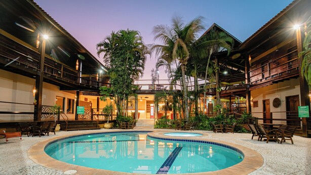 Área de piscina com duas piscinas, deck de madeira e espreguiçadeiras.