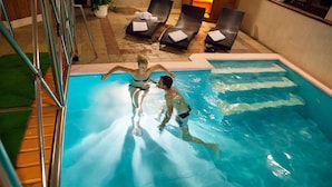 Piscina com escada de metal, cadeiras de descanso e piso cerâmico.
