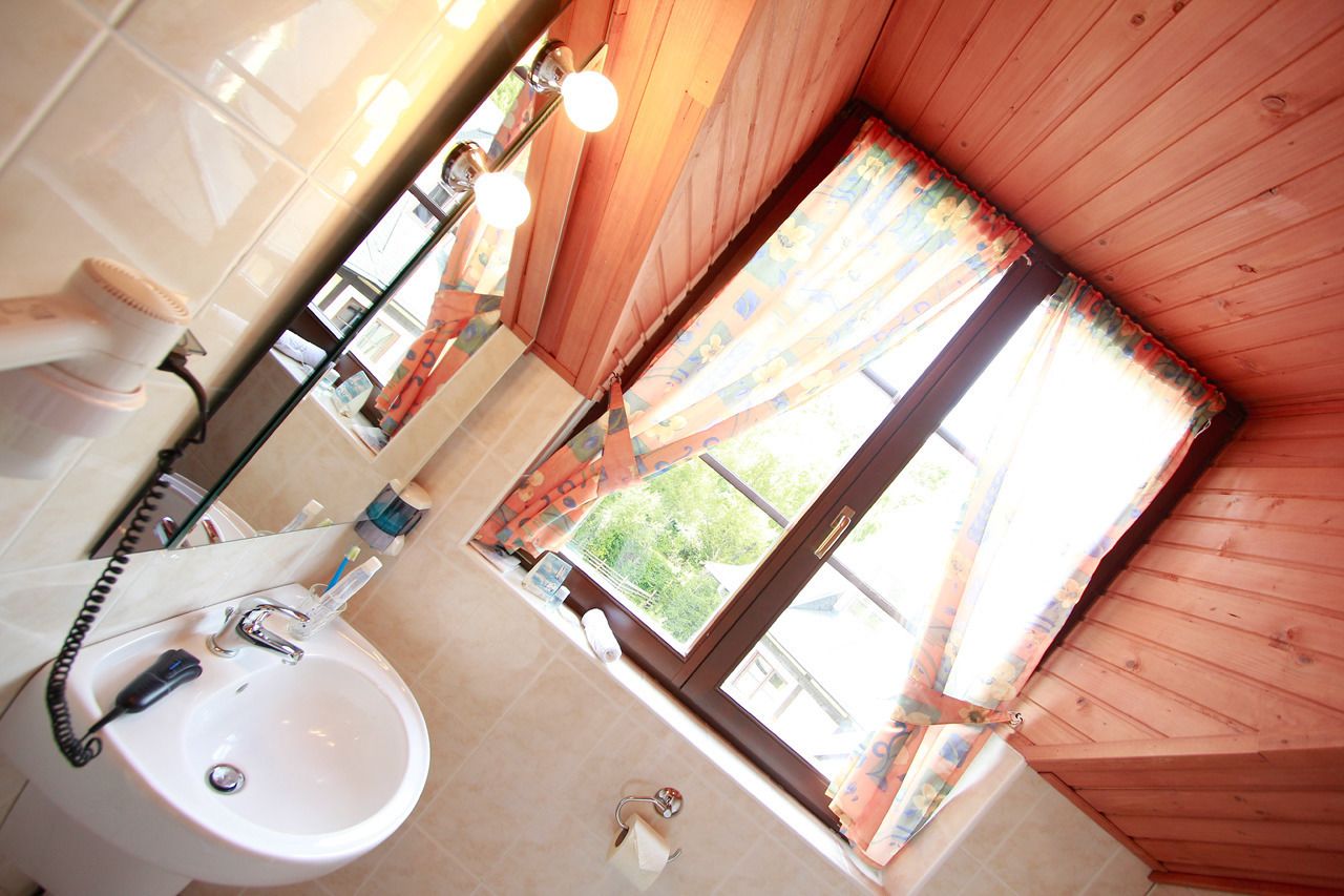 Casa de banho com lavatório, espelho e janela com cortinas.