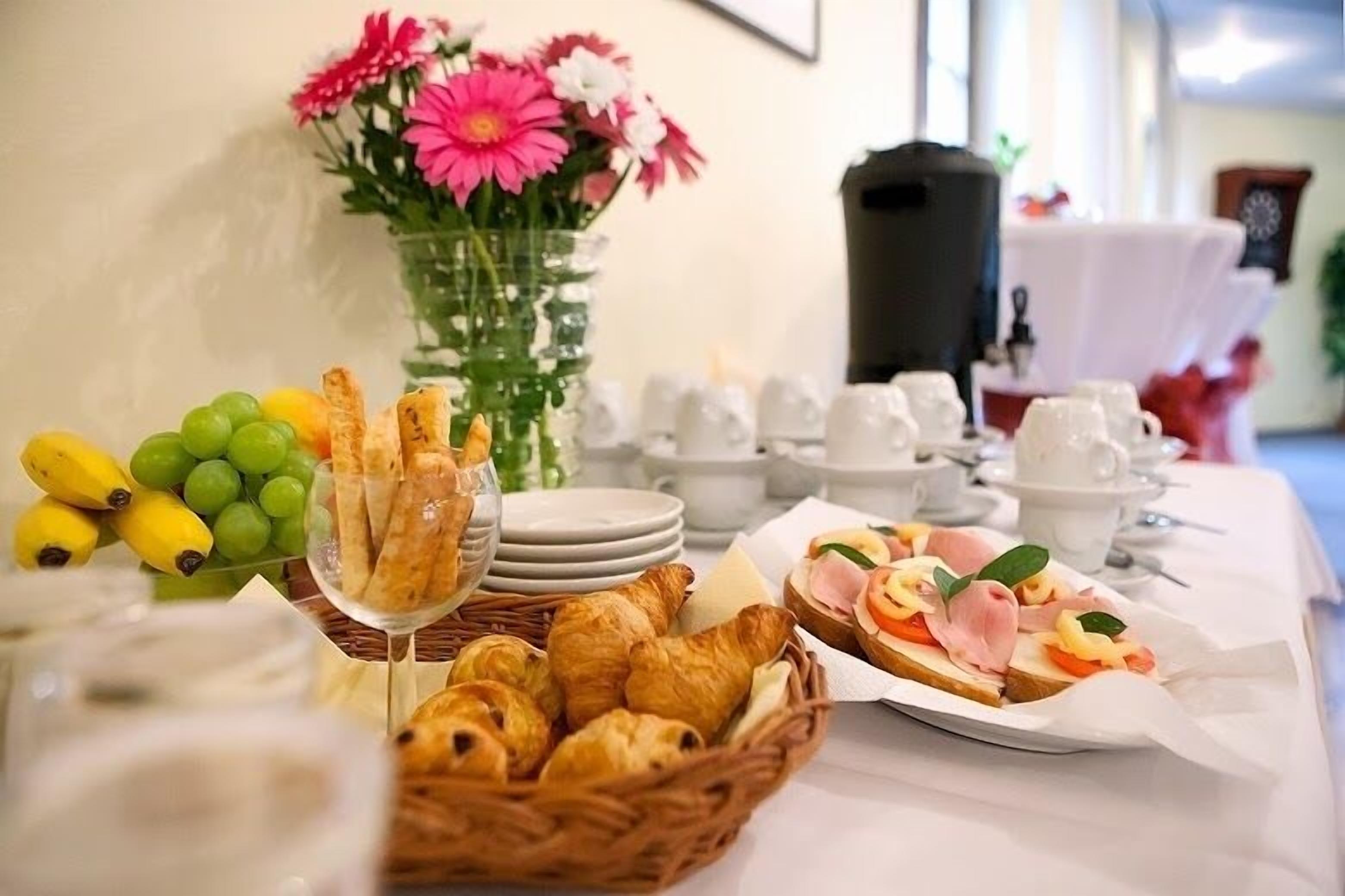 Buffet de café da manhã com croissants, pães, bananas, uvas e uma variedade de doces.