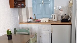 Uma cozinha compacta com porta azul, um armário de madeira sobre a pia, uma pequena mesa de jantar com cadeiras e um vaso com planta.