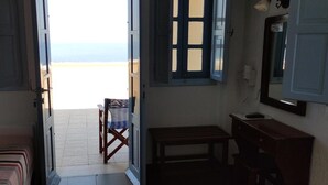 Quarto com vista para a praia, uma pequena mesa, um banco e um espelho na parede.