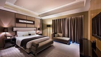 Quarto de hotel moderno com uma cama grande, um sofá, uma televisão de tela plana e uma janela ampla com cortinas.