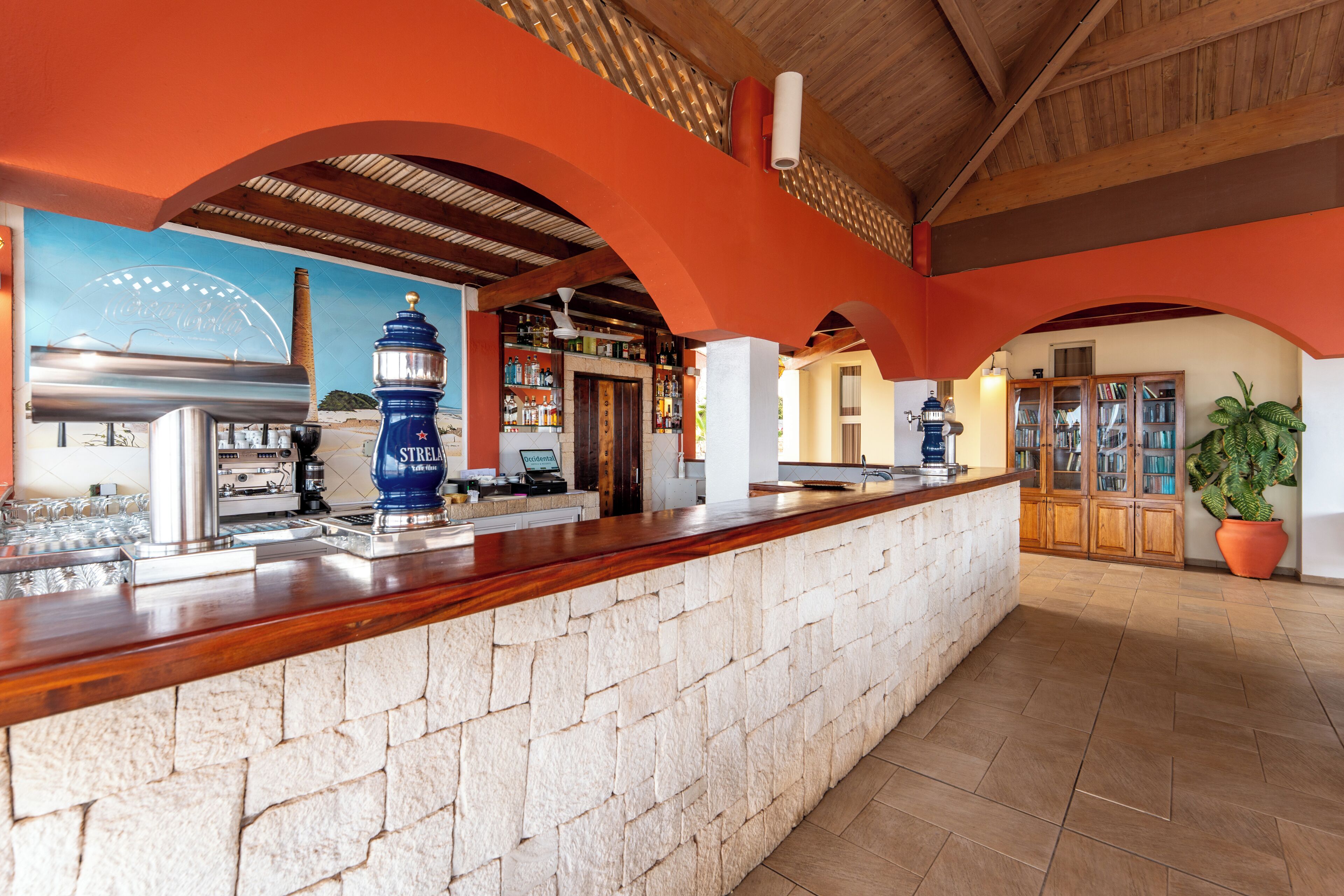 Uma área de bar com balcão de pedra, um objeto decorativo azul e um mural da Coca-Cola.