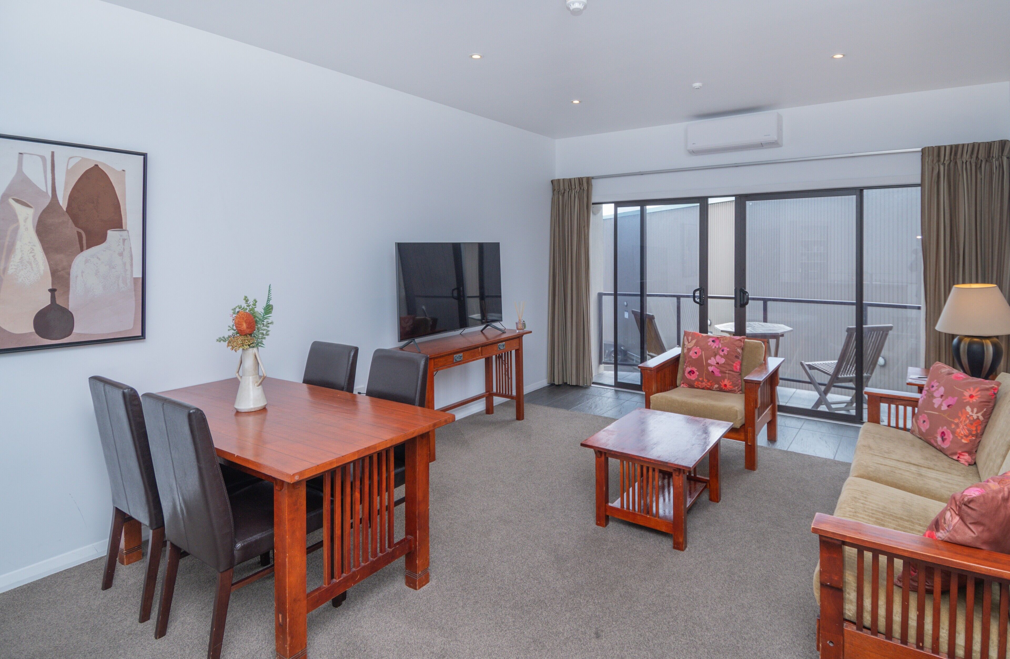 Quarto de hotel moderno com área de refeições, sofá, TV e varanda com cortinas.