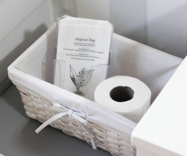 Uma cesta de vime branca com um saco de lixo e um rolo de papel higiênico.