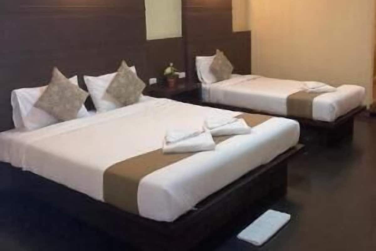 Quarto de hotel com duas camas, cada uma com travesseiros e um cobertor, uma mesinha de cabeceira e um aparelho de ar condicionado na parede.