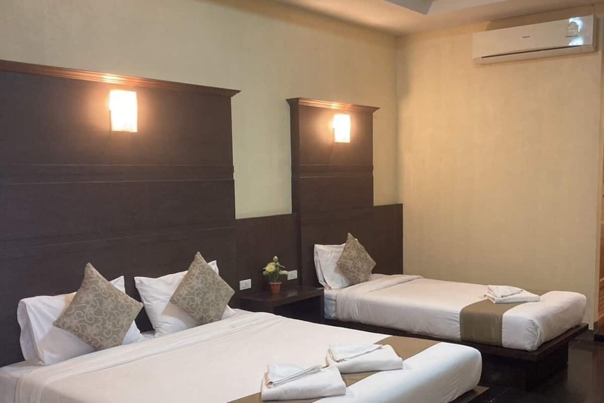 Quarto de hotel com duas camas, cada uma com roupa de cama branca e almofadas decorativas. Tem uma mesinha de cabeceira com uma pequena mesa e um vaso de flores. O quarto tem um design moderno com cabeceiras de madeira escura e uma luminária no teto.