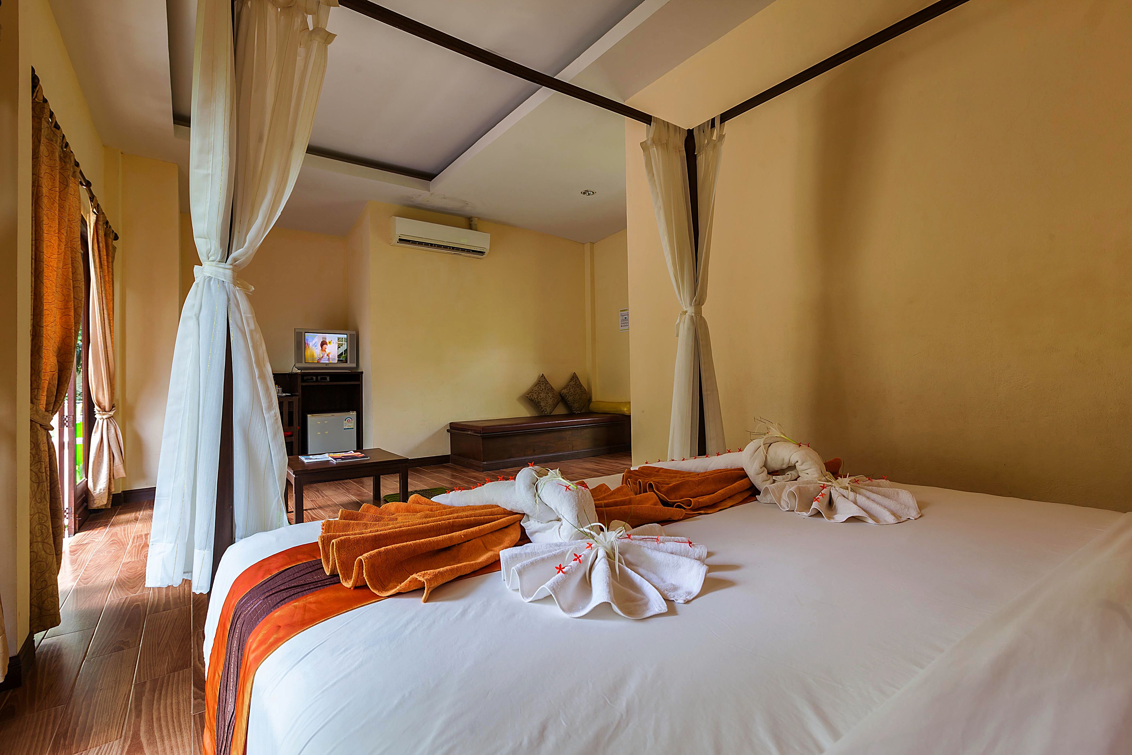 Quarto de hotel com cama, cortinas, televisão, escrivaninha e mesa de cabeceira.
