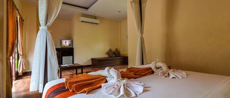 Quarto de hotel com cama, cortinas, televisão, escrivaninha e mesa de cabeceira.