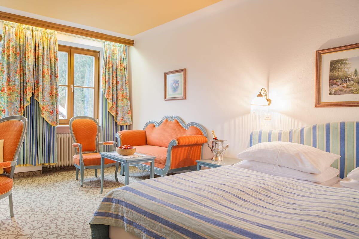 Quarto de hotel com cama, poltrona, mesa e janela com cortinas.