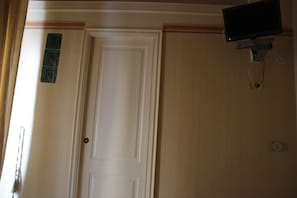 Quarto de hotel com porta fechada, televisão presa à parede e tomada.