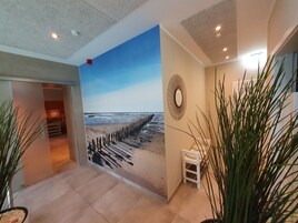 Um corredor com um mural de praia, um banquinho branco pequeno e plantas altas.