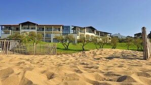 Um hotel na praia com várias varandas, uma praia de areia e uma área arborizada com gramado.