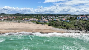 Uma vila costeira com uma praia de areia, casas com telhados vermelhos e vista para o oceano.