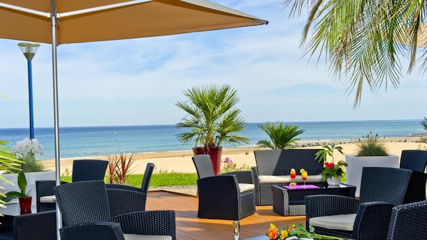 Uma área de estar ao ar livre com móveis de vime e vista para a praia.