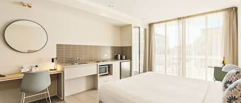 Quarto de hotel com cama, secretária, cadeira e cozinha compacta.