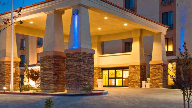 Edifício Holiday Inn Express & Suites com entrada coberta, pilares de pedra e um mastro.