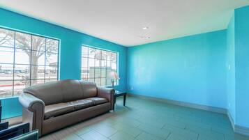 Quarto com paredes verde-água, um sofá de couro marrom e uma pequena mesa com abajur.