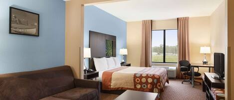 Quarto de hotel com cama, escrivaninha, cadeira, sofá e televisão.