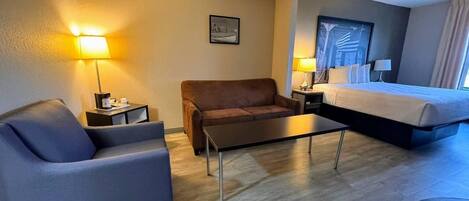 Quarto de hotel com cama, sofá, mesa de centro e duas luminárias.