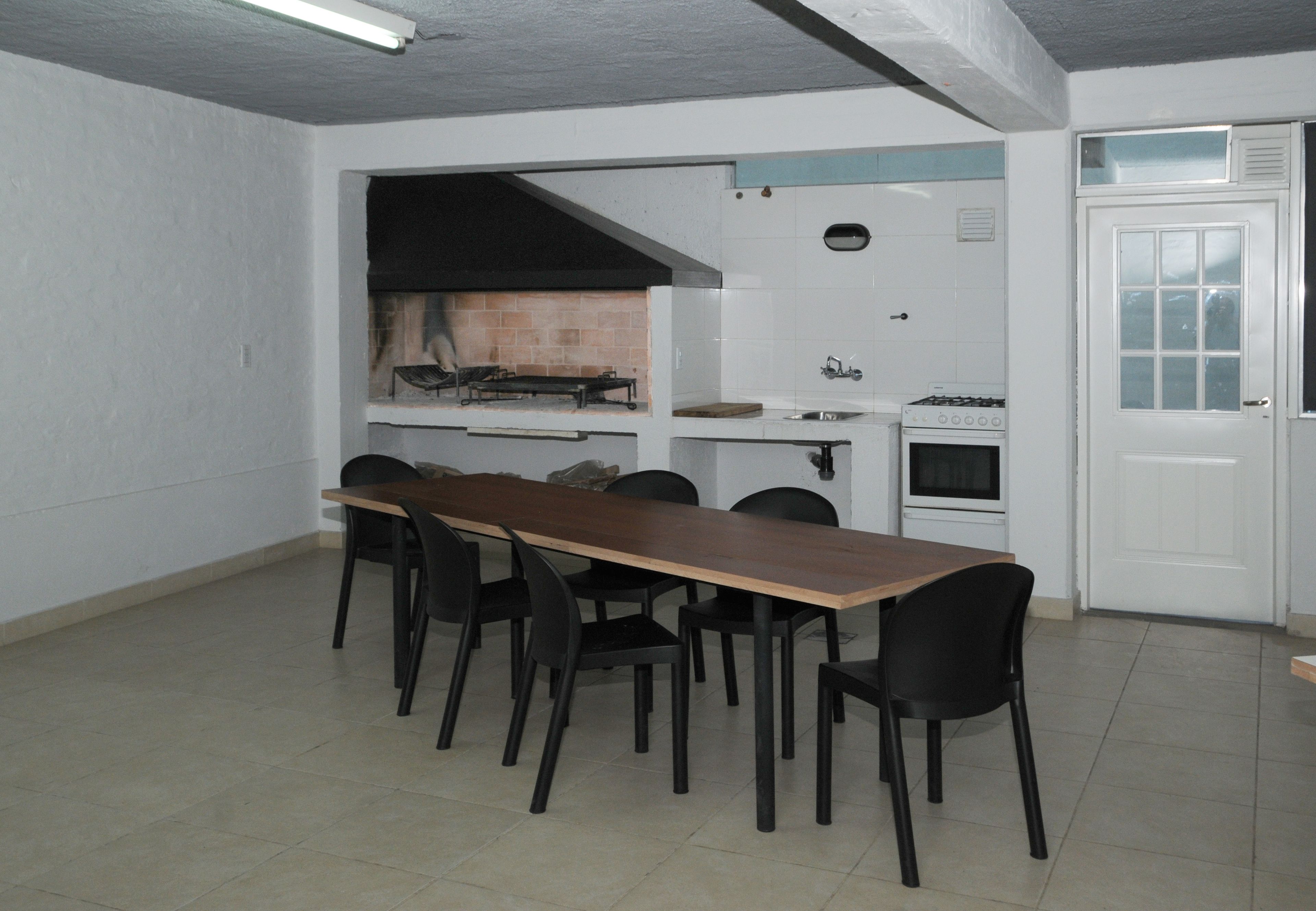 Cozinha com fogão, pia e coifa preta. Há uma mesa de madeira com cadeiras.