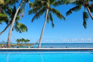 Piscina azul translúcida com palmeiras e vista para o oceano.