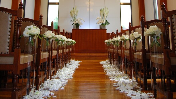 Interior de igreja com bancos de madeira, altar de madeira e uma cruz.
