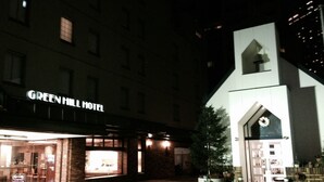 Exterior do Hotel Green Hill com fachada de tijolos, uma grande entrada iluminada e um guirlanda de Natal na porta.
