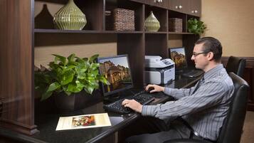 Um homem trabalhando numa mesa com um laptop, uma impressora e uma planta em vaso.