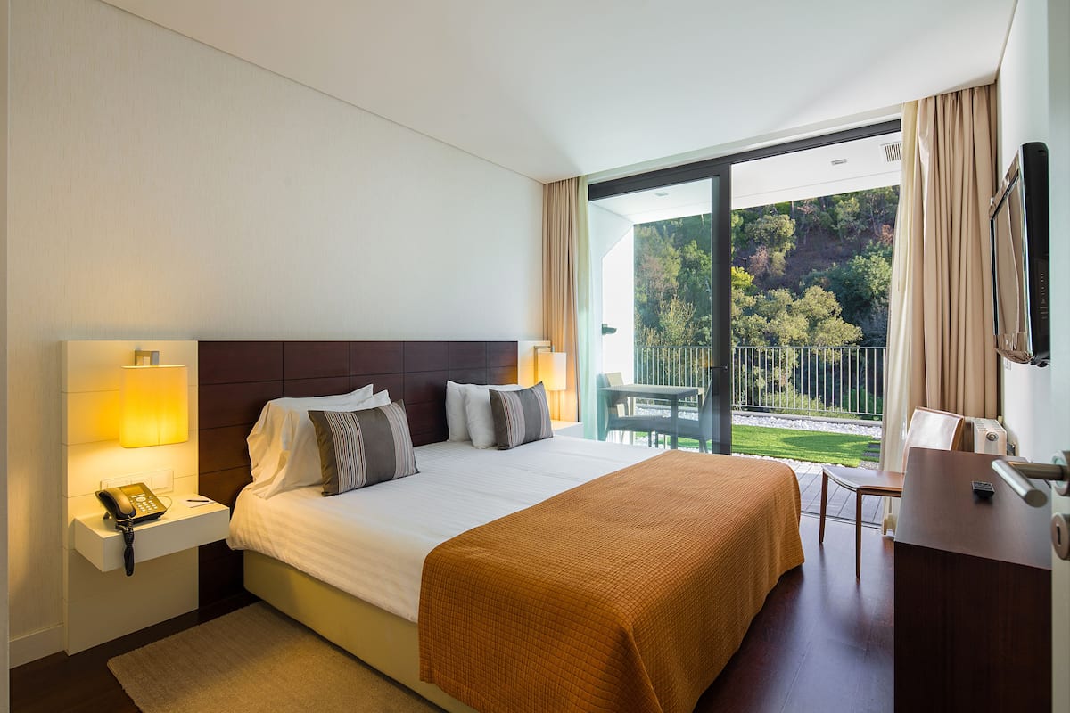 Quarto de hotel com uma cama grande, luminárias de cabeceira, uma escrivaninha e vista para o exterior.